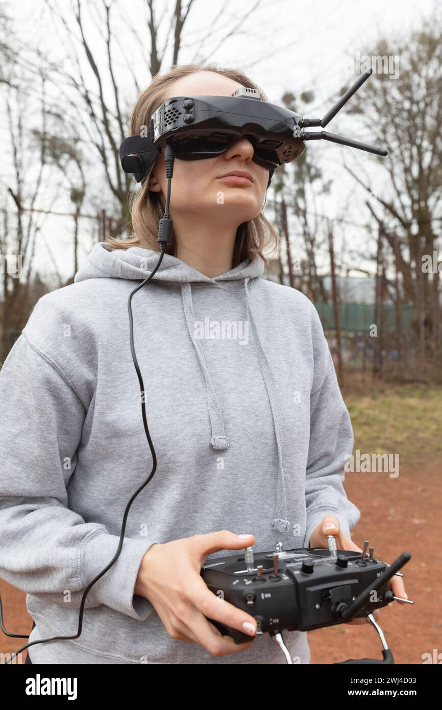 A young woman wears virtual reality goggles and holds a remote control ...
