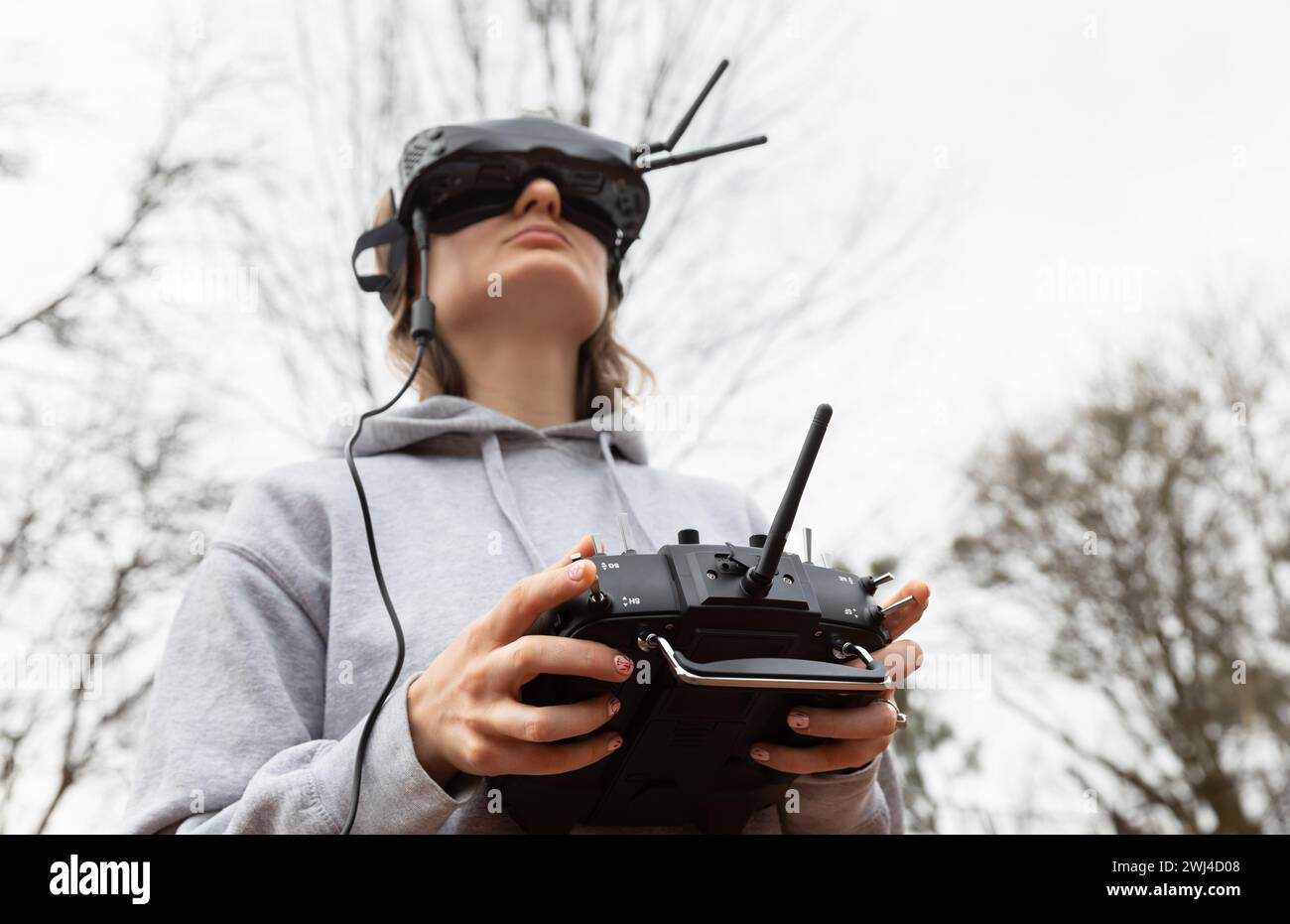 A young woman wears virtual reality goggles and holds a remote control ...