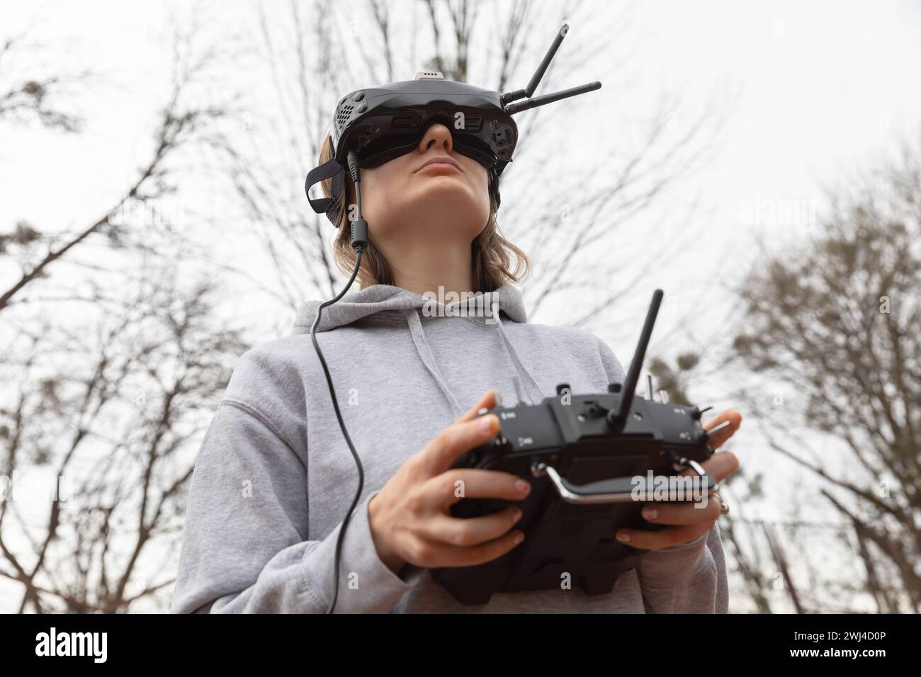 A young woman wears virtual reality goggles and holds a remote control ...