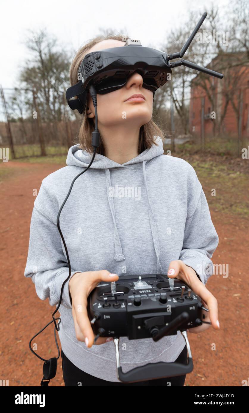 A young woman wears virtual reality goggles and holds a remote control ...