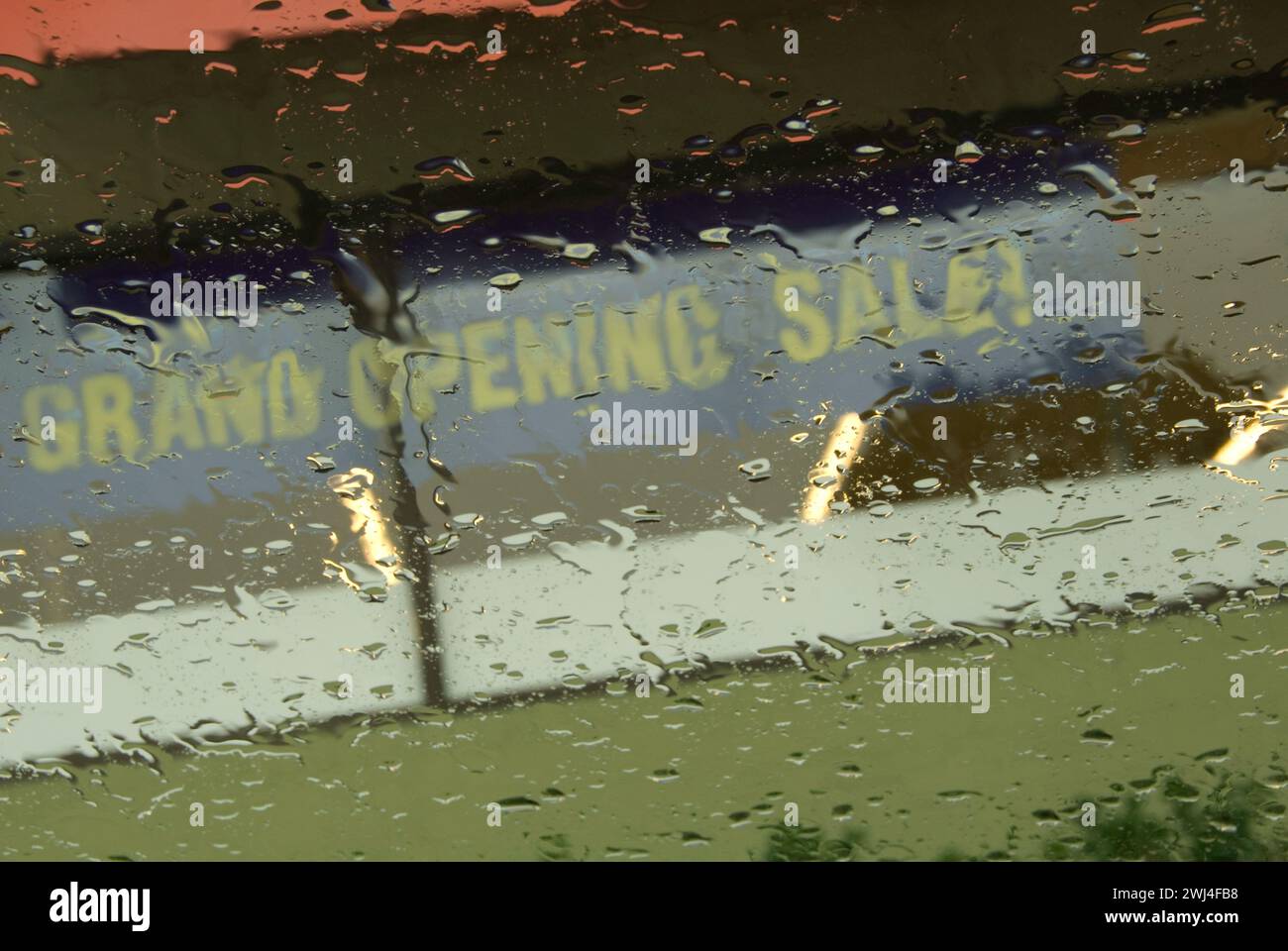 "Grand Opening Sale" sign on store seen through rain on car window ...