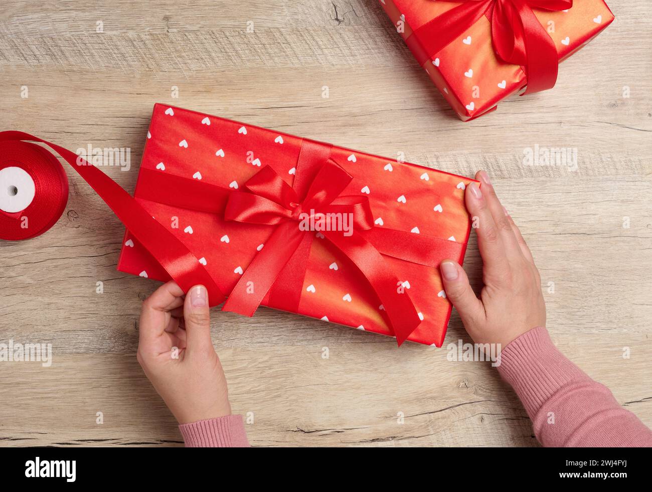 Female hands holding a gift box with a red ribbon on a brown background. View from above Stock ...