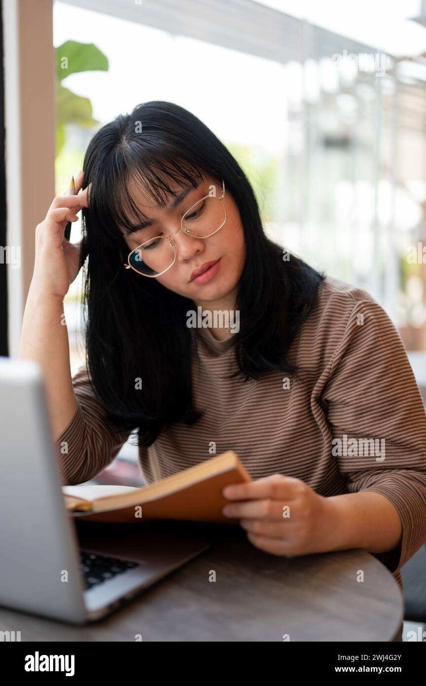 A serious and thoughtful young Asian female college student is reading ...