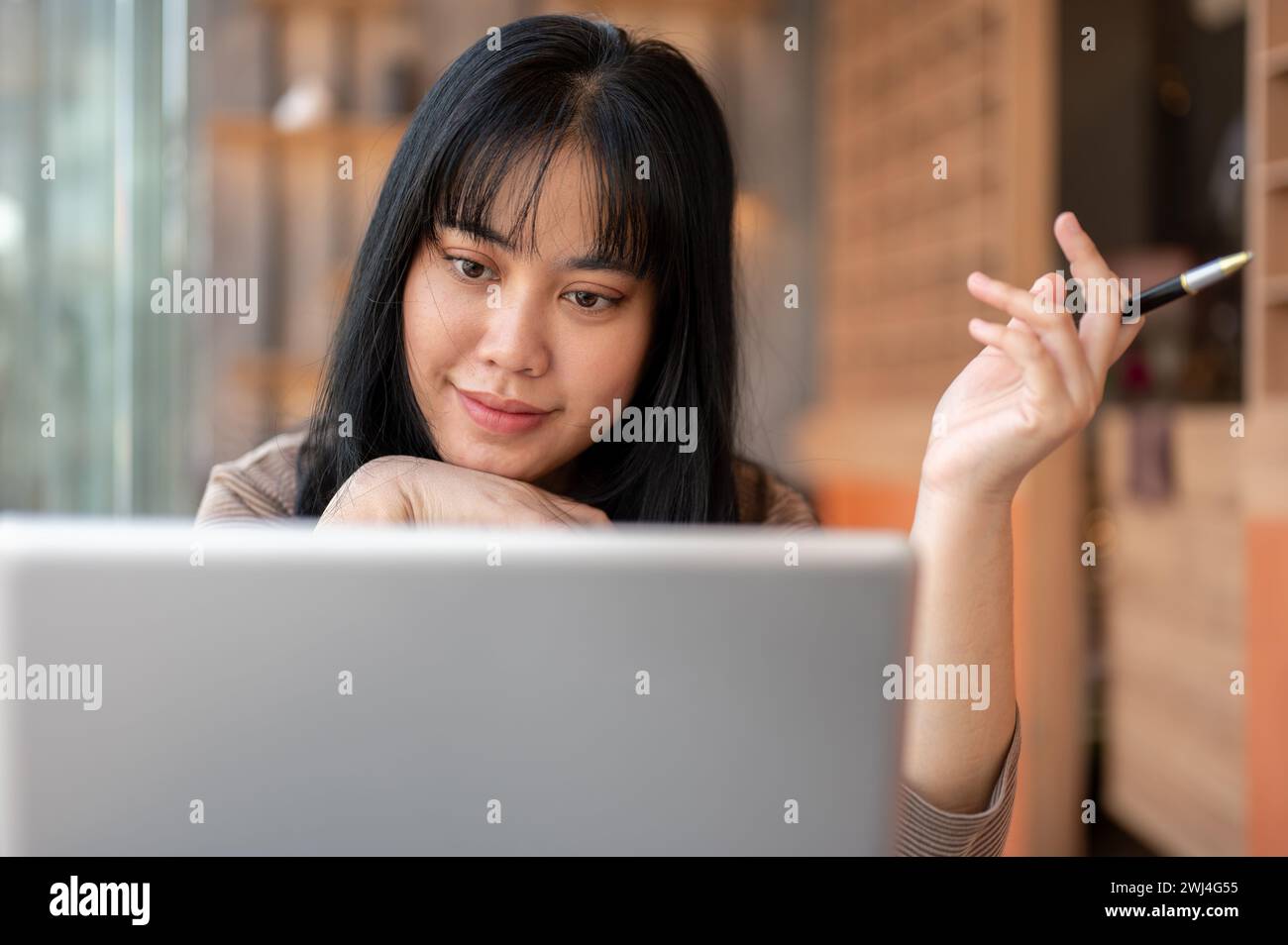 A beautiful Asian woman is working remotely at a cafe co-working space ...