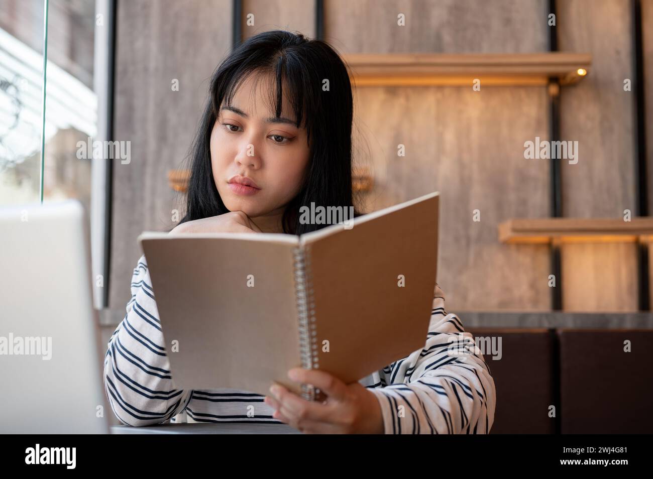 A serious, thoughtful Asian woman is concentrating on reading a book ...
