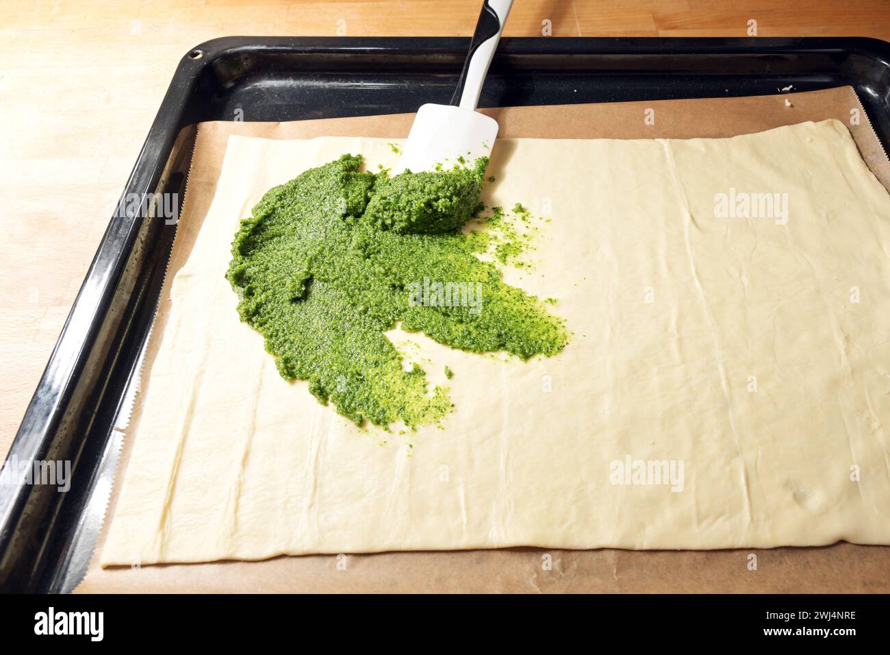 Raw puff pastry dough on baking paper and a tray is spread with ...