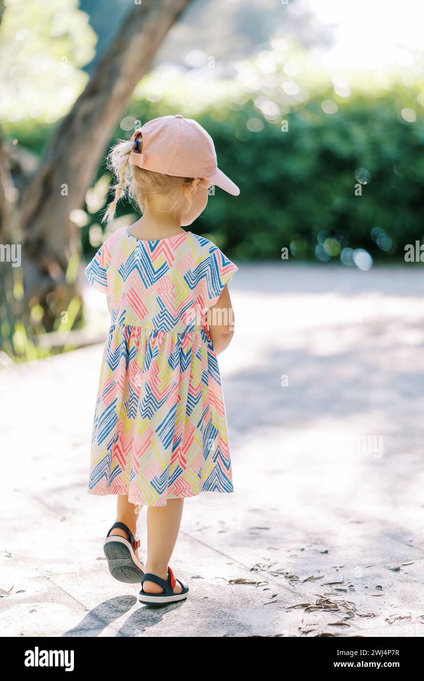 Little girl walks along a path in a sunny garden. Back view Stock Photo ...