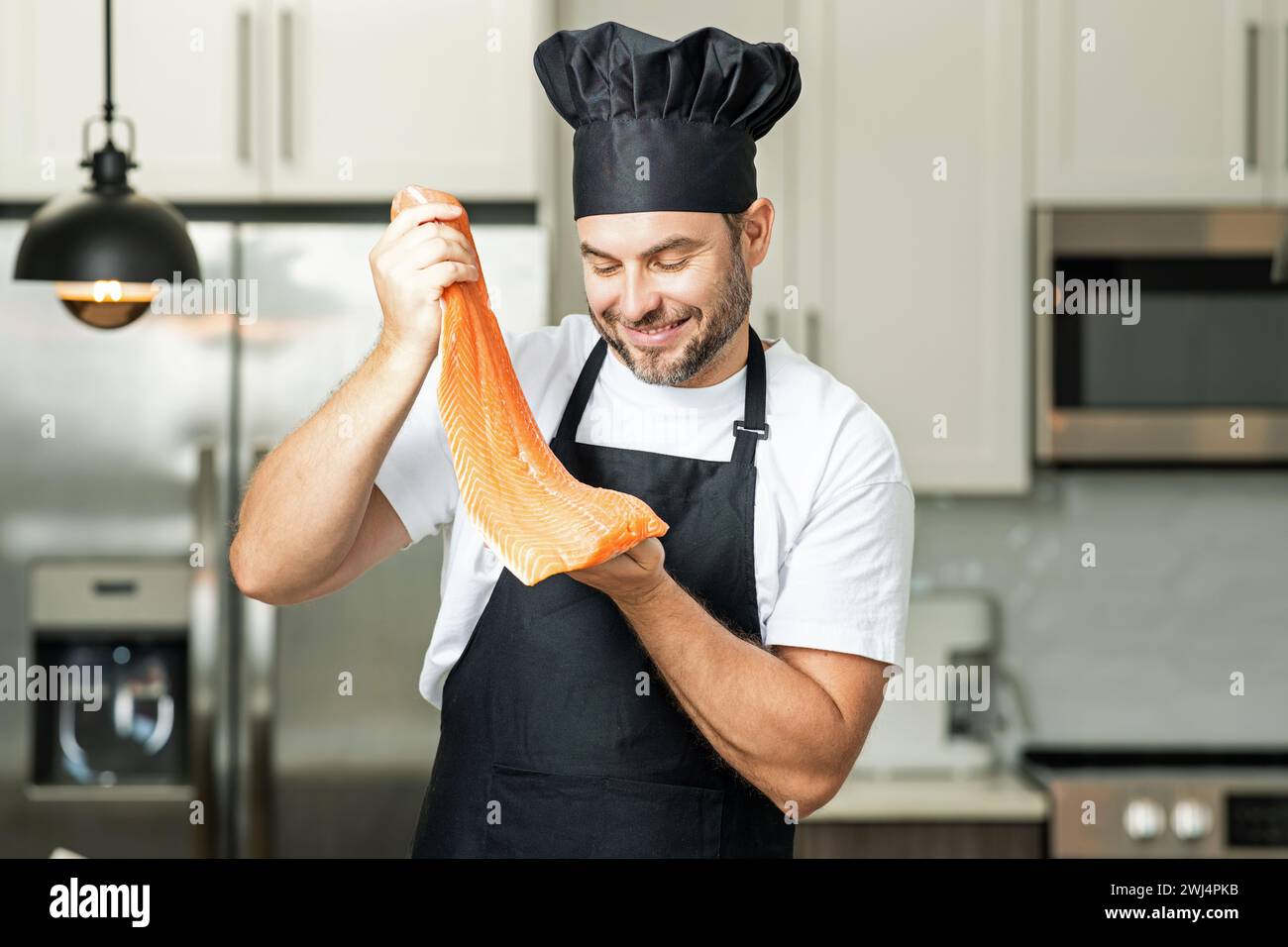 Chef with raw meat fish salmon fillet on kitchen. Chef man in uniform ...