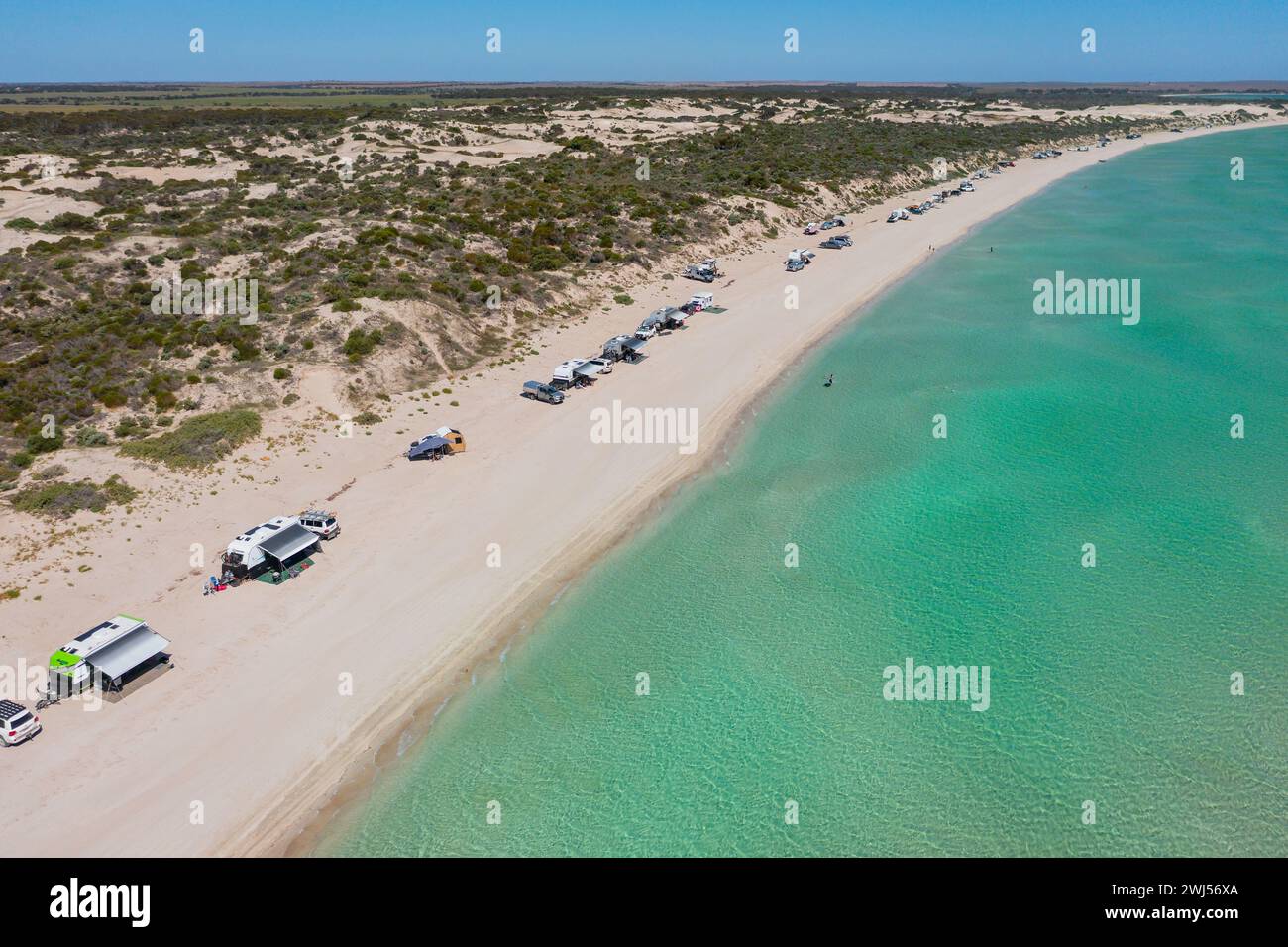Aerial view of a line of caravans camping on a white sandy beach next ...