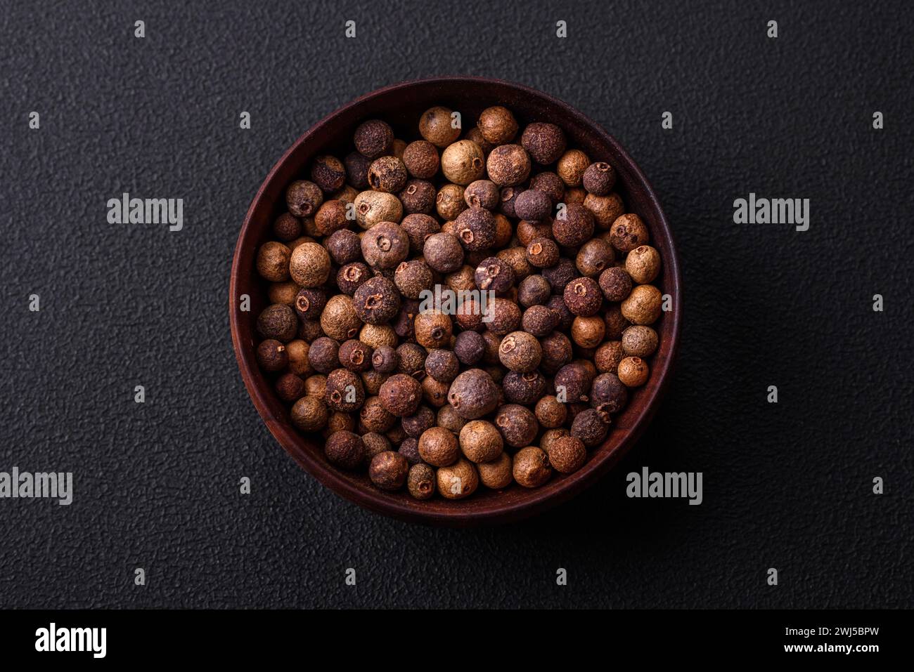 Spice allspice brown color not ground in a wooden saucer on a dark ...