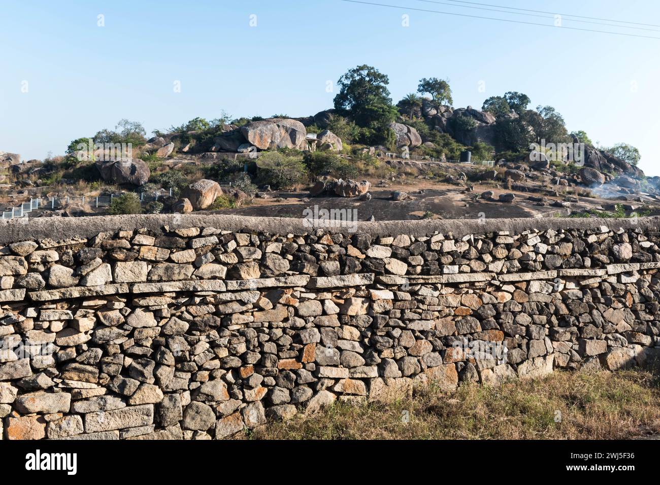 A rustic stone wall at the base of a rocky landscape sets a serene ...