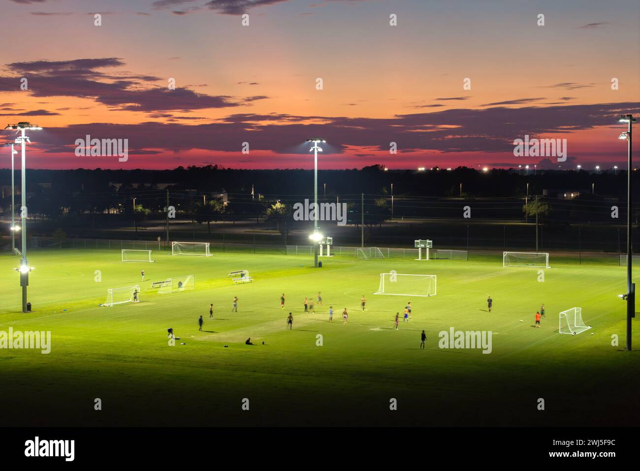 People playing soccer game on illuminated public stadium at sunset ...