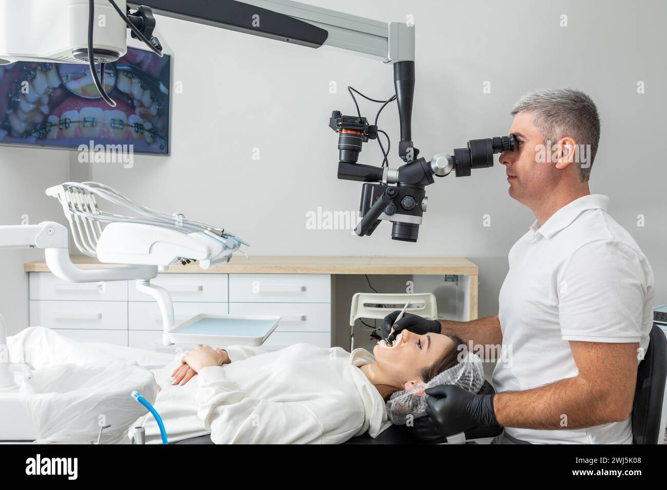 Dentist using dental microscope treating patient teeth at dental clinic ...