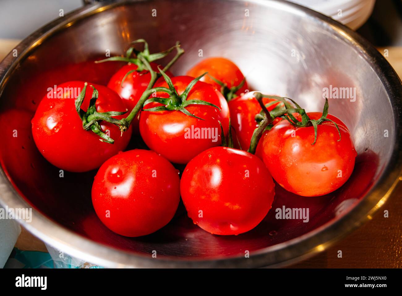 Bright red ripe tomatoes on the vine in a shiny stainless steel bowl ...