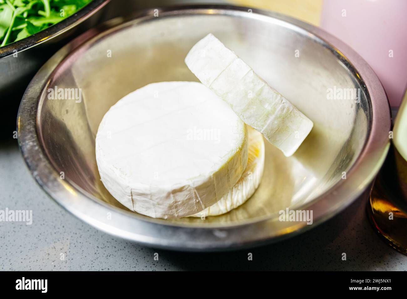A whole wheel of Brie cheese alongside a sliced piece on a metal bowl ...
