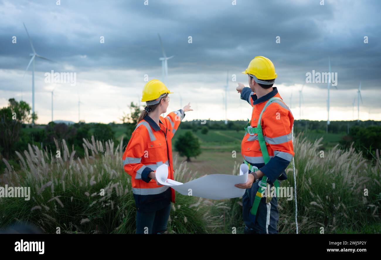 Two engineers working on a construction site with wind turbines in the ...
