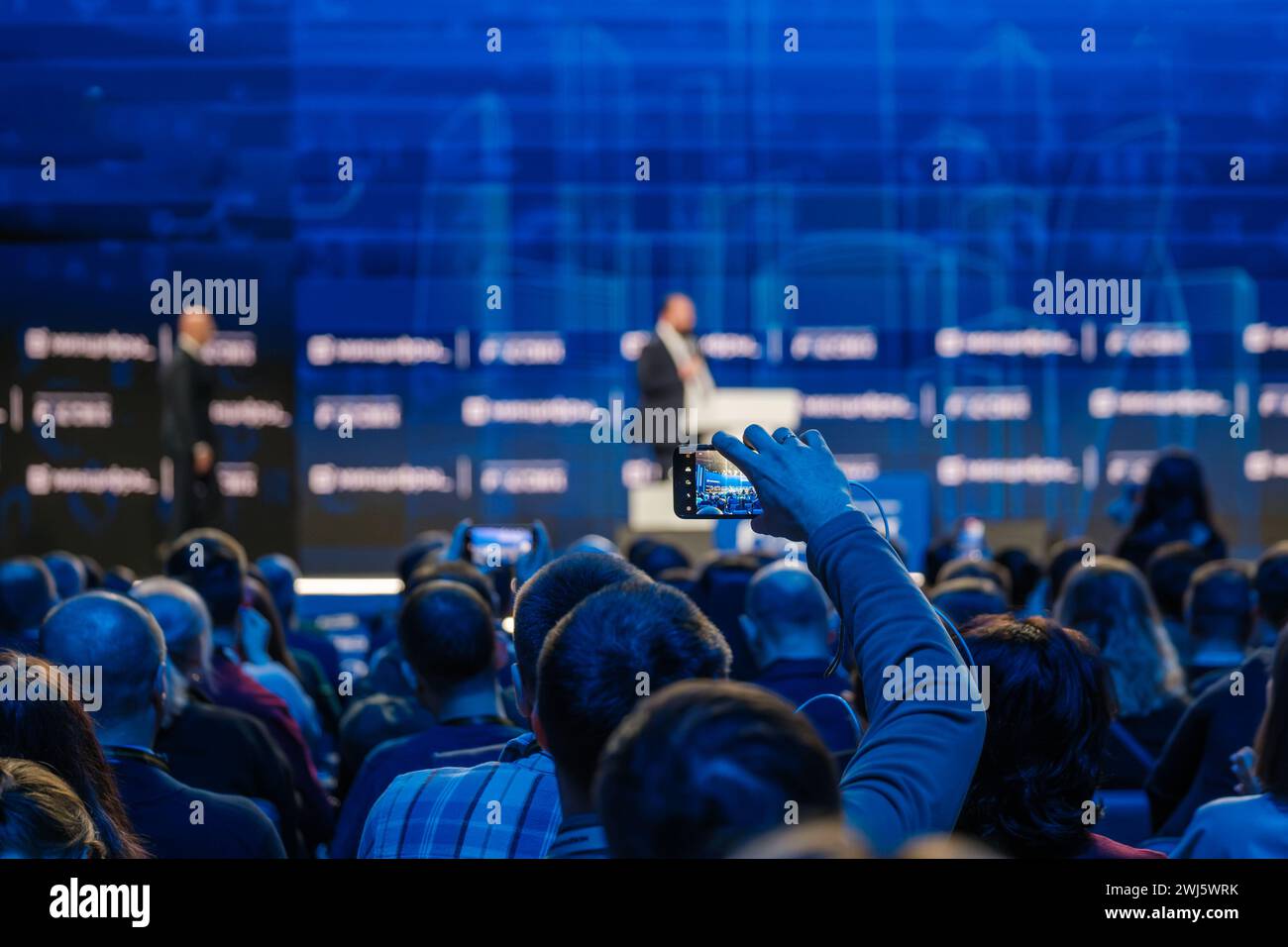 Business event attendees recording speaker on stage giving a ...