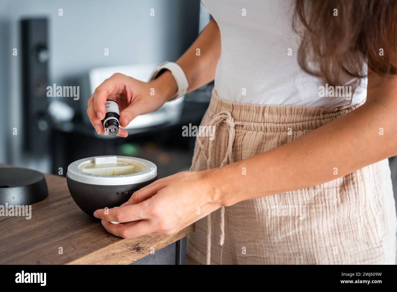 Woman adding oil to the grey aroma oil diffuser on light table at home ...