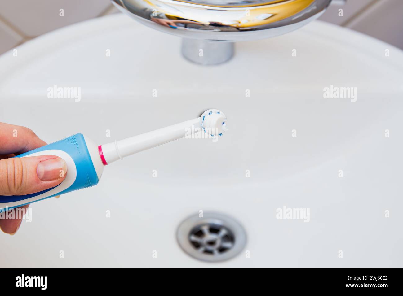 Hand holding electric toothbrush with toothpaste in bathroom near ...