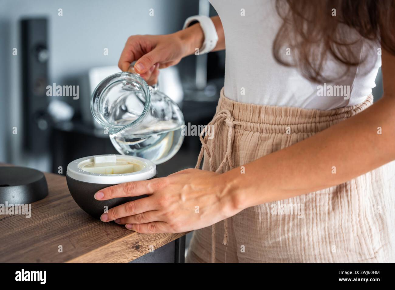 Woman adding water to the grey aroma oil diffuser on light table at ...