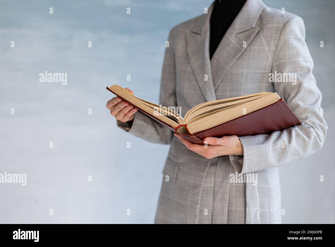 An unrecognizable woman holds a large brown book in her hands. business ...