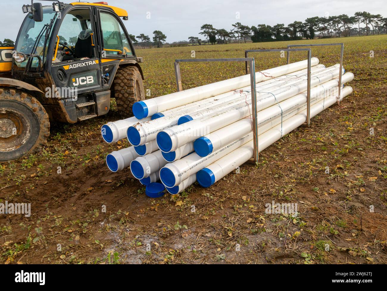 Plastic water pipeline sections in field next to JCB Agrixtra vehicle ...