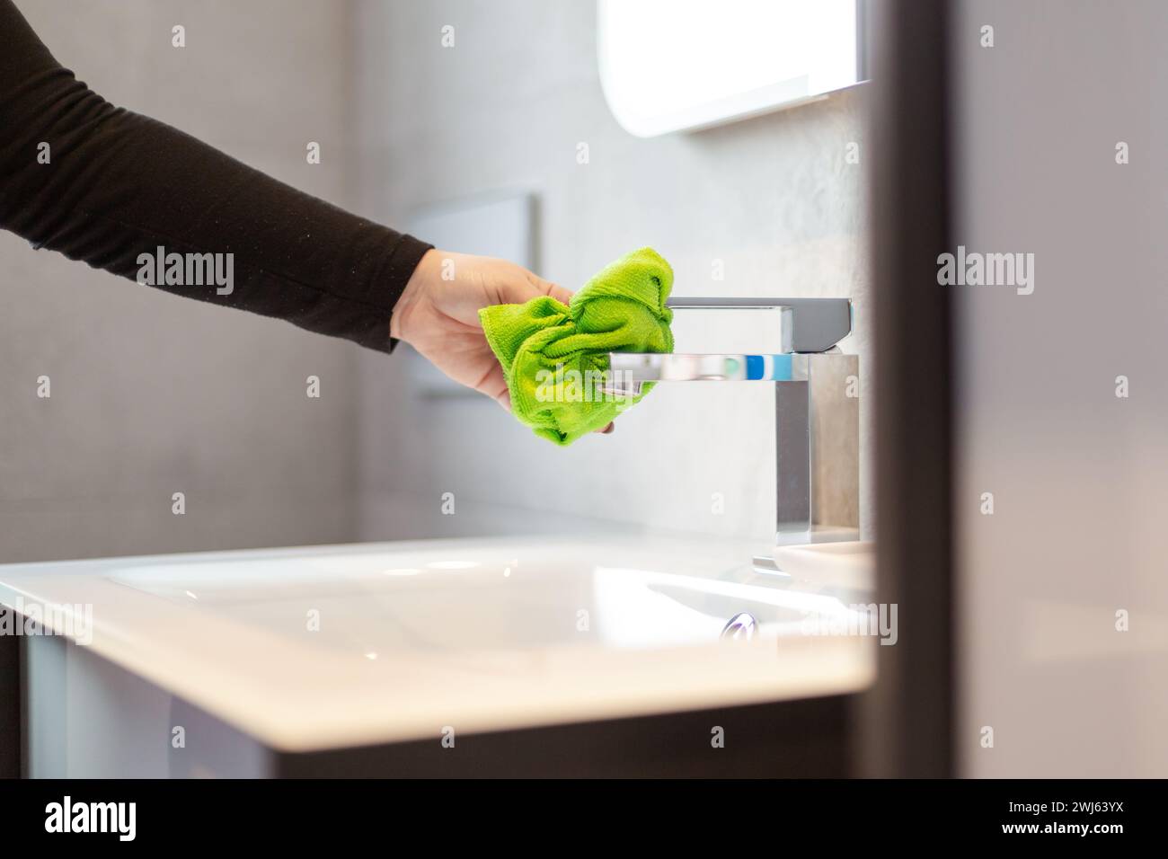 Cleaning water tap and basin in a modern bathroom. Candid low angle ...