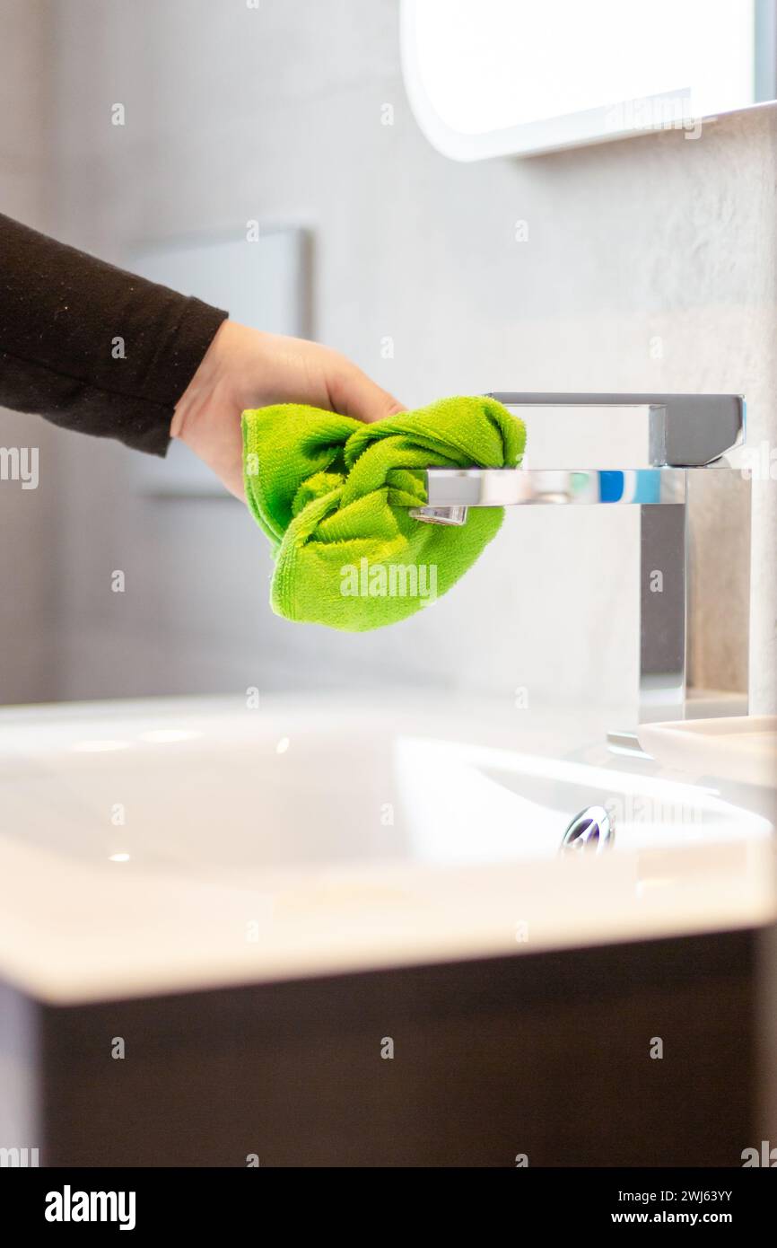 Cleaning water tap and basin in a modern bathroom. Candid low angle ...