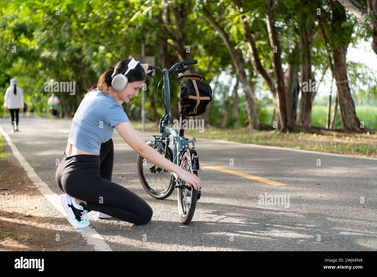 A young woman listens to music with headphones while checking the readiness of her bicycle ...