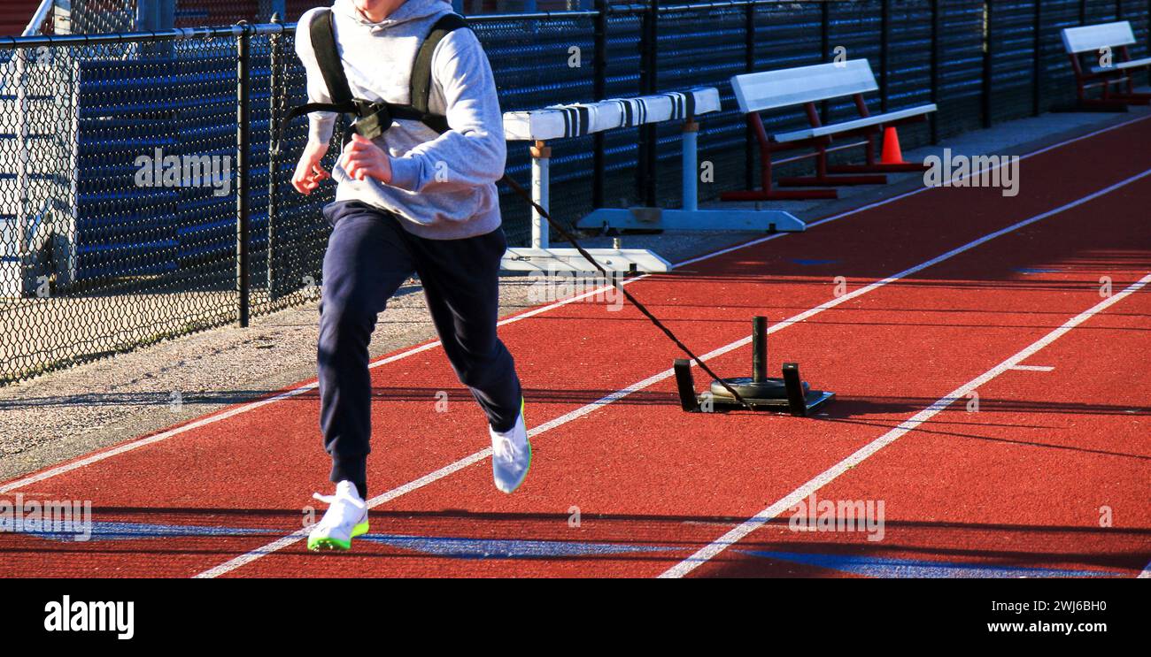 Front view of a high school boy pulling a sled with weight on a track ...