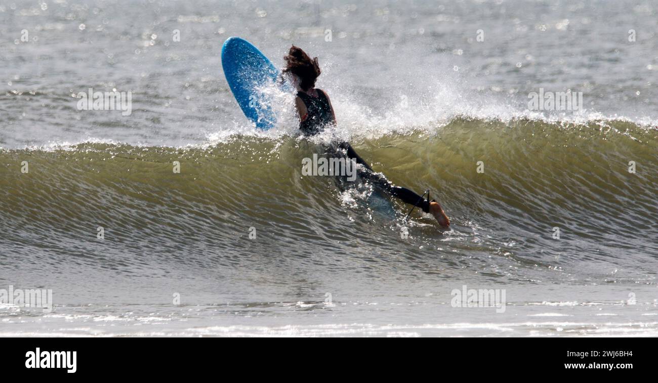 Rear view of a male Surfer in a wetsuit splashing through a wave ...