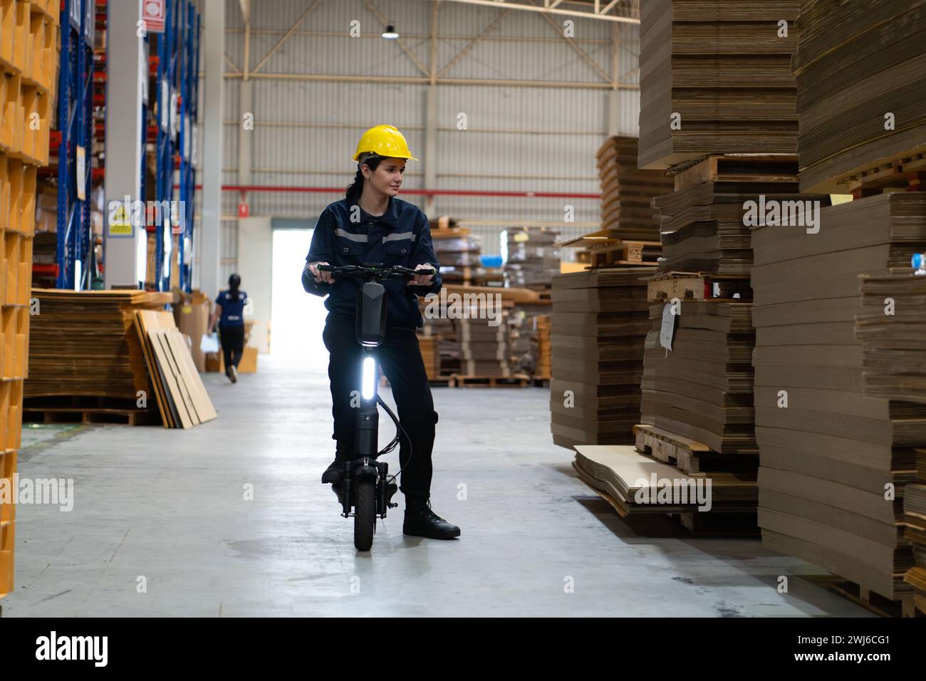 Young female warehouse worker ridding with electric scooter in ...