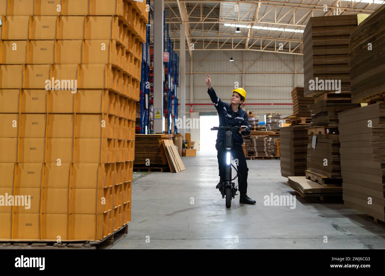 Young female warehouse worker ridding with electric scooter in ...