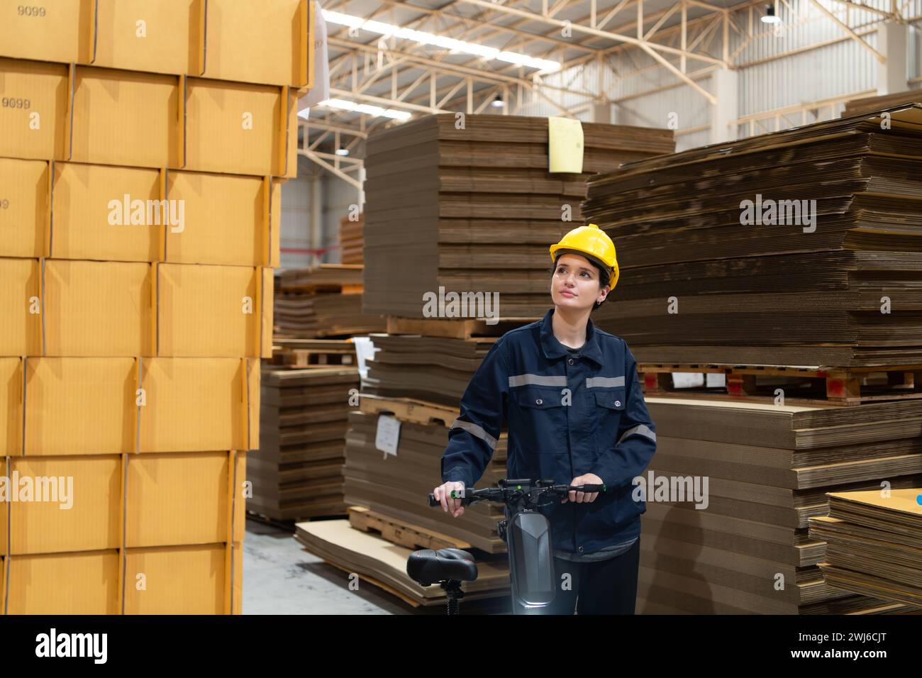 Young female warehouse worker ridding with electric scooter in ...