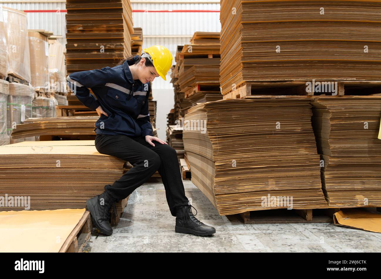 Warehouse worker sitting on the floor in front of stack of cardboard ...