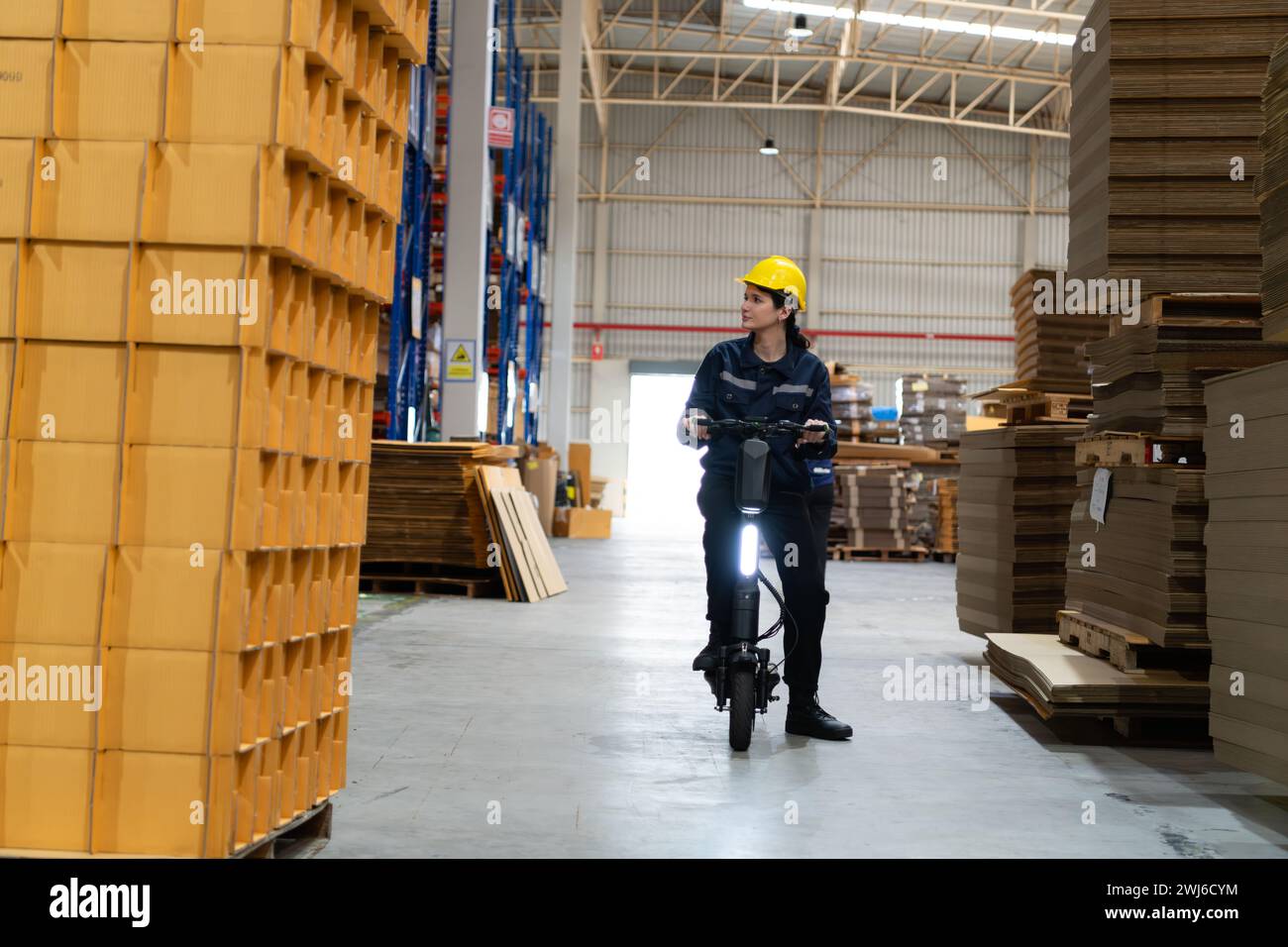 Young female warehouse worker ridding with electric scooter in ...