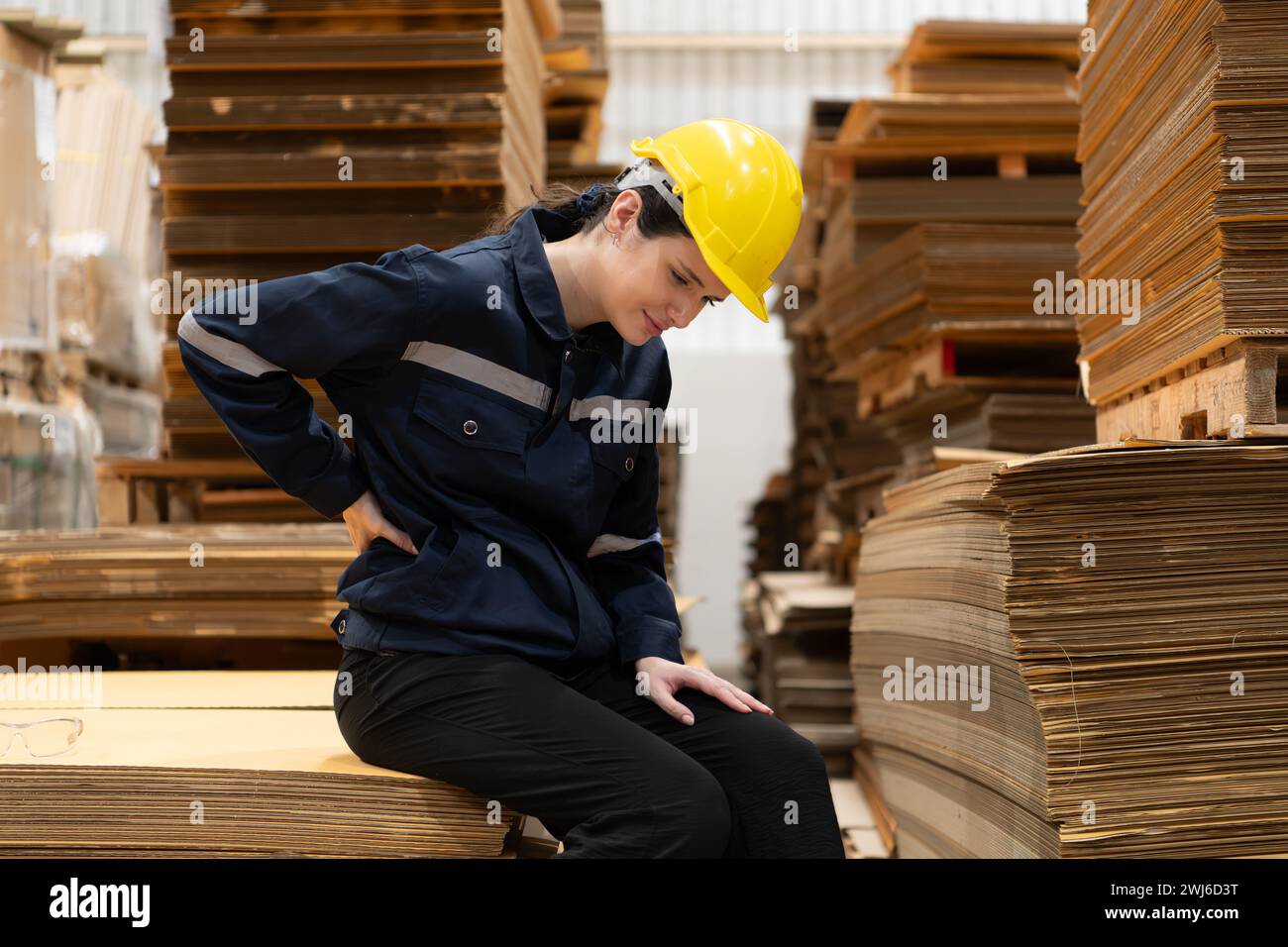Warehouse worker sitting on the floor in front of stack of cardboard ...