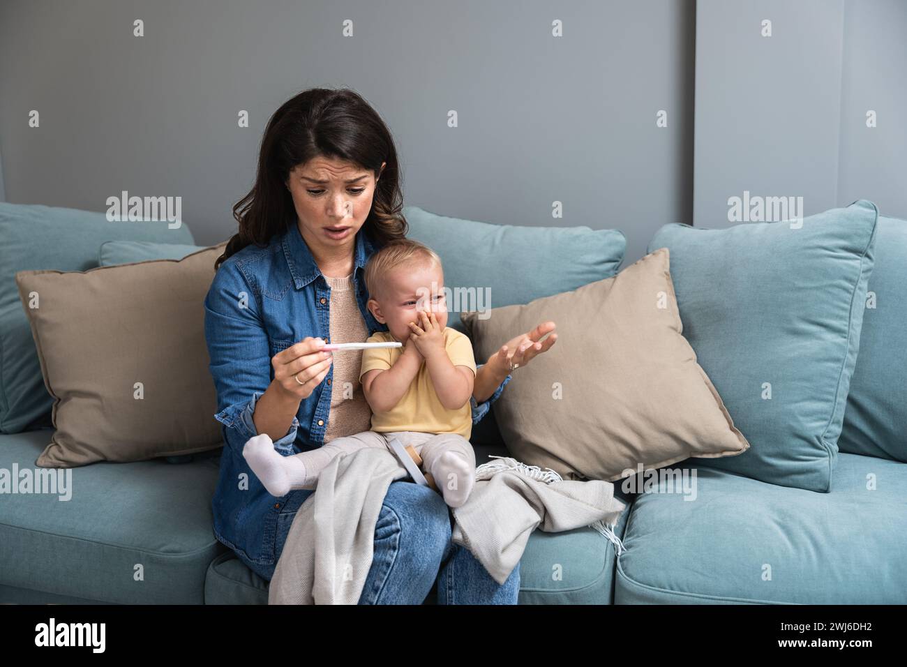 Young shocked mother holds a baby in her lap and a pregnancy test in ...