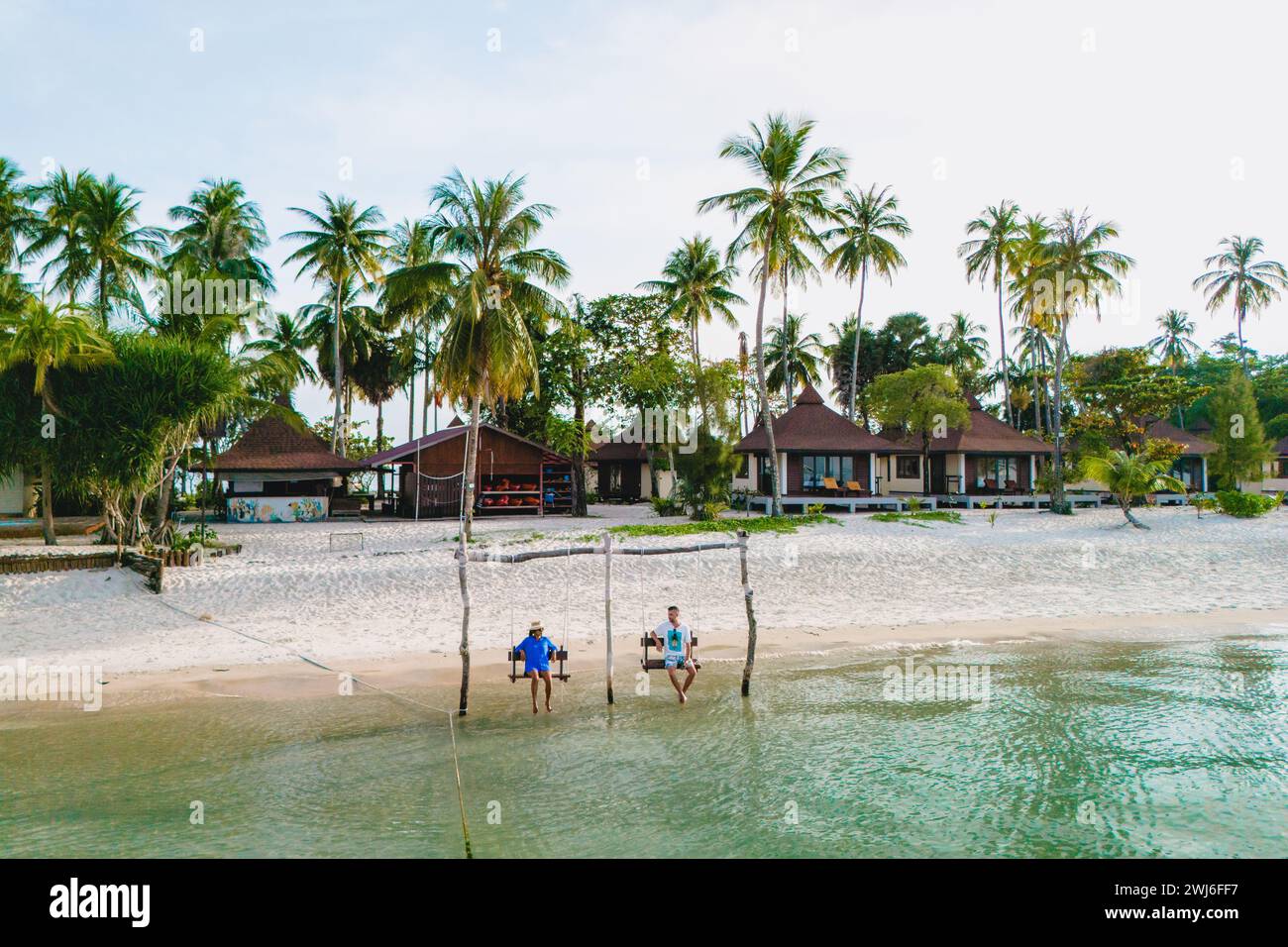 A couple of men and woman on a swing at the beach of Koh Muk Thailand ...