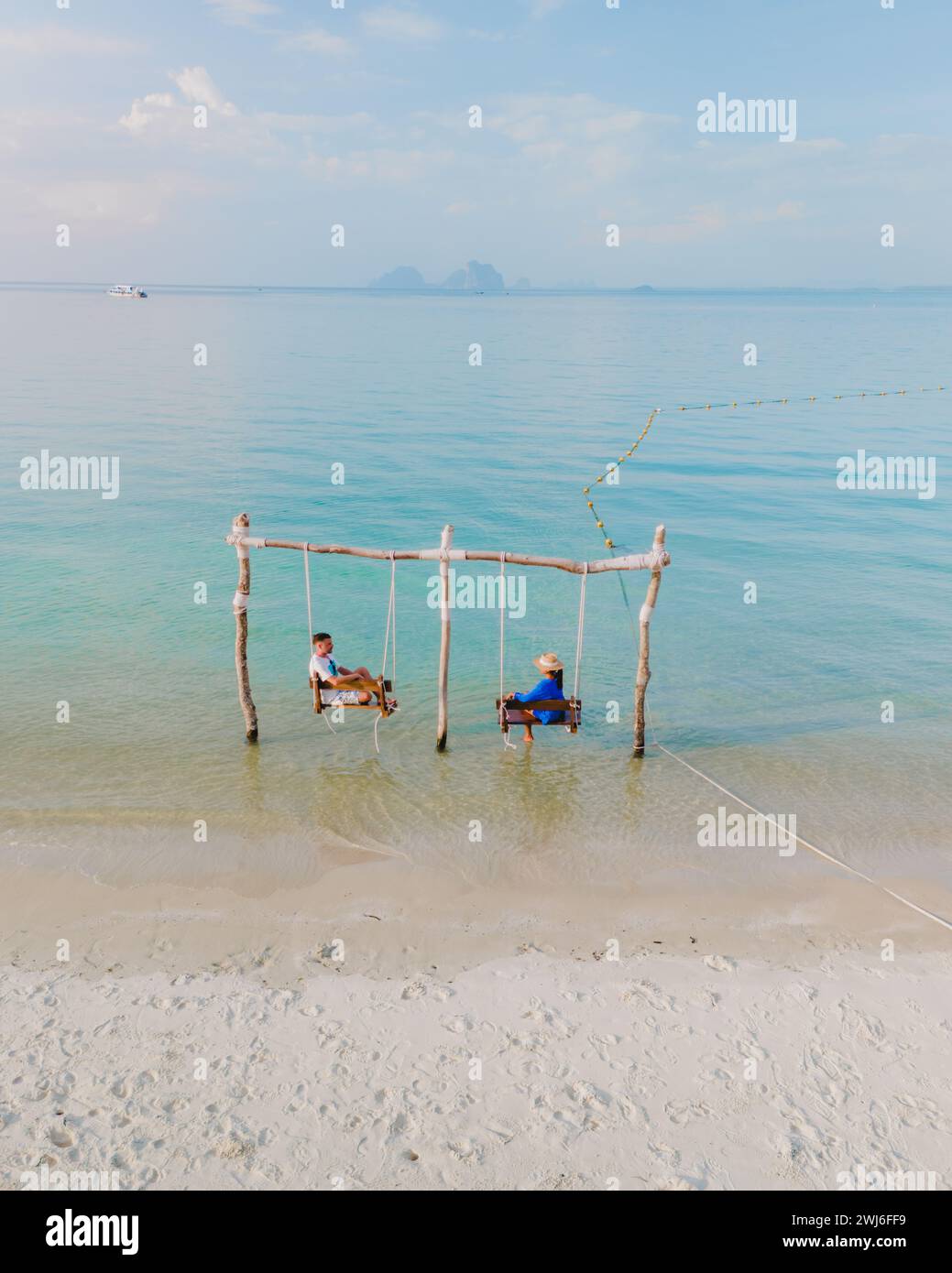 A couple of men and woman on a swing at the beach of Koh Muk Thailand ...