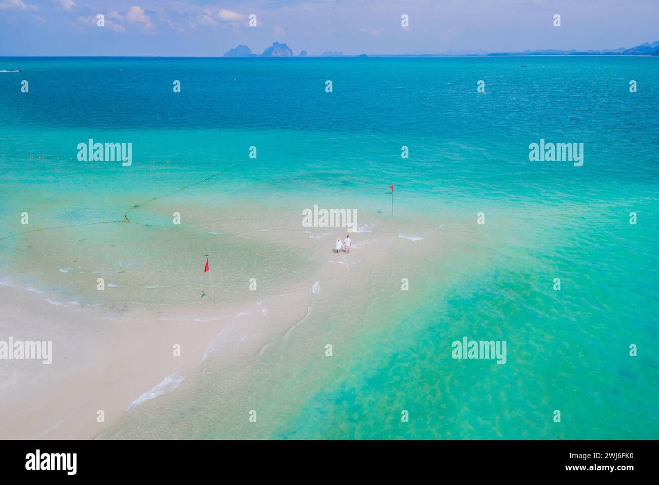 A couple of men and woman walking at a sandbar in the ocean of Koh Muk Thailand or Koh Mook ...
