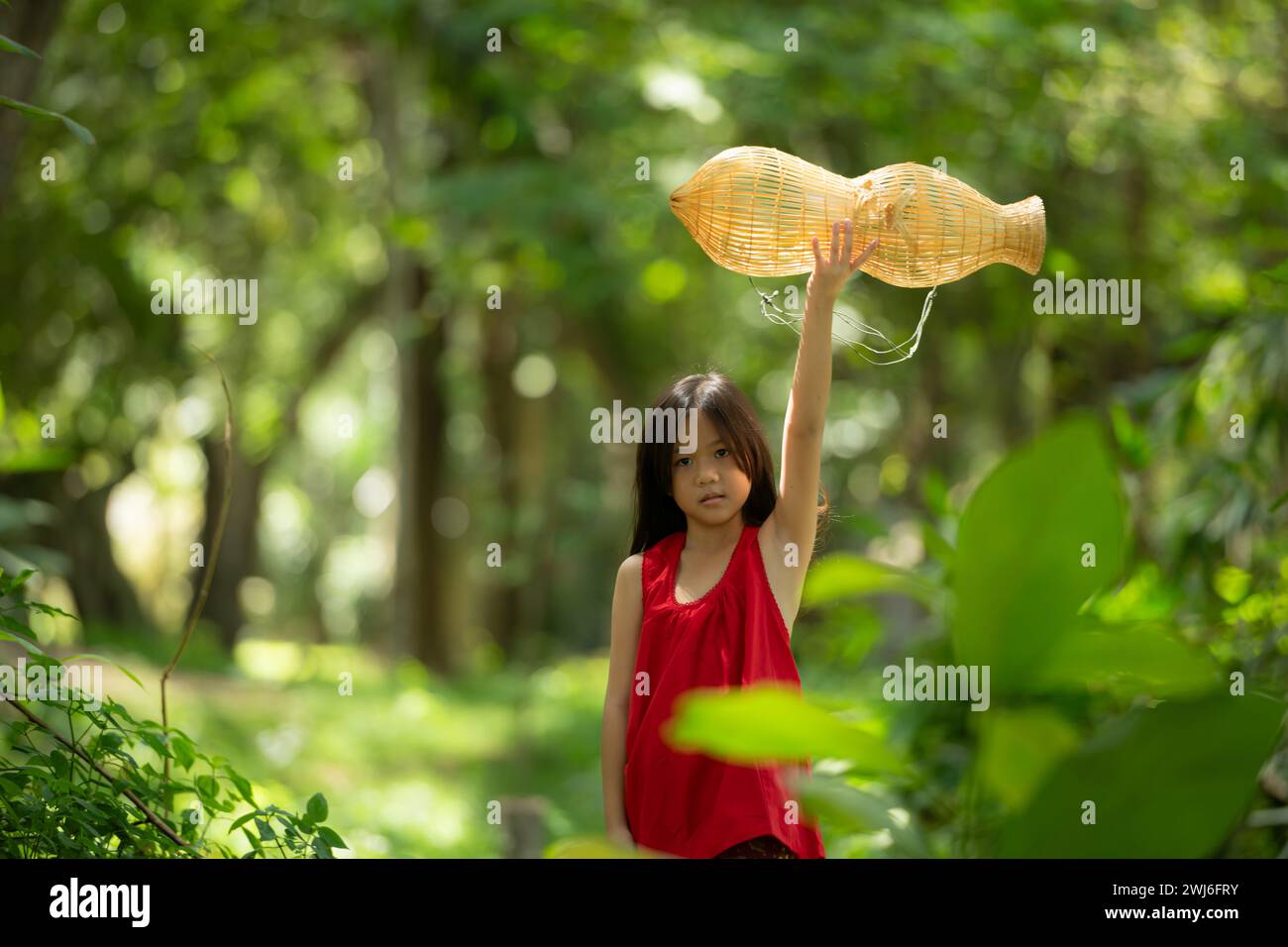 Little asian girl in red dress holding fishing equipment in the forest, Rural Thailand living ...