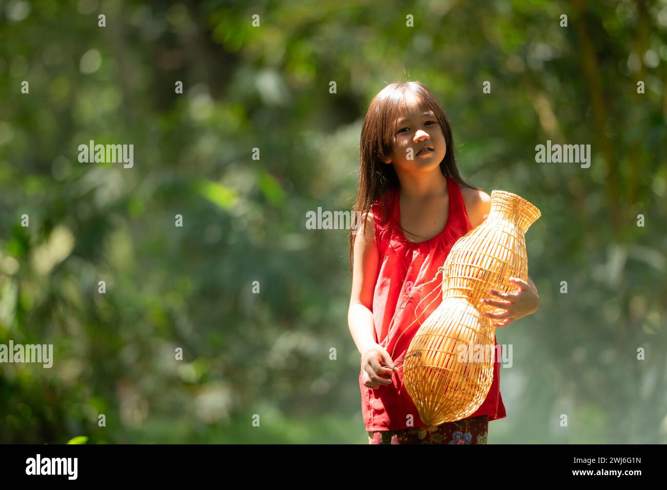 Little asian girl in red dress holding fishing equipment in the forest, Rural Thailand living ...