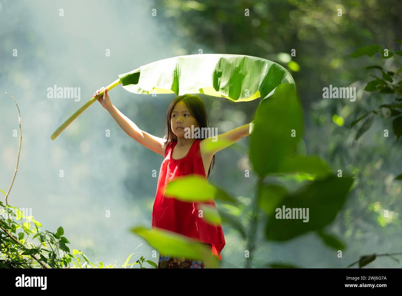 Little asian girl in red dress holding fishing equipment in the forest, Rural Thailand living ...