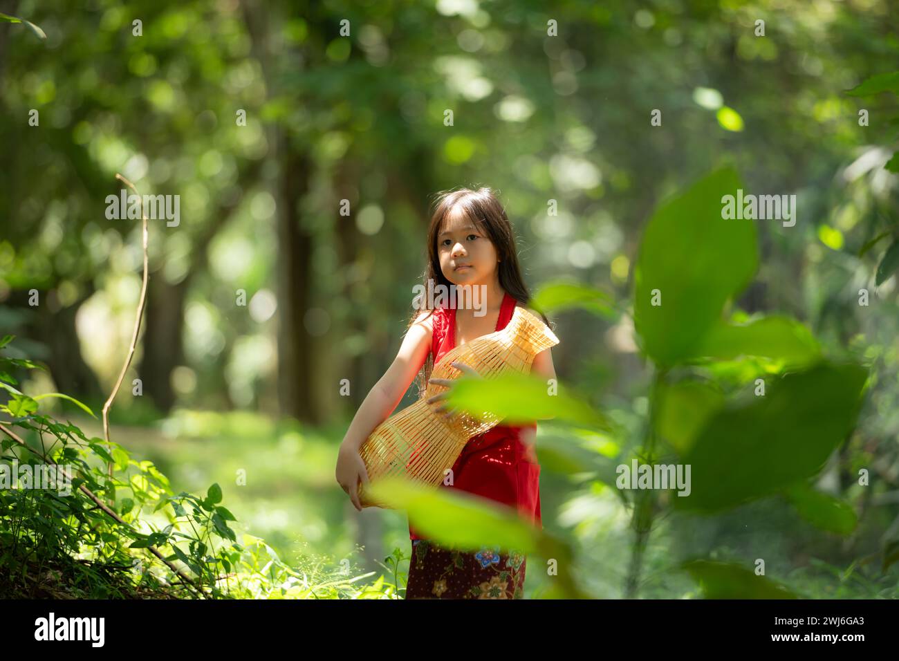 Little asian girl in red dress holding fishing equipment in the forest, Rural Thailand living ...