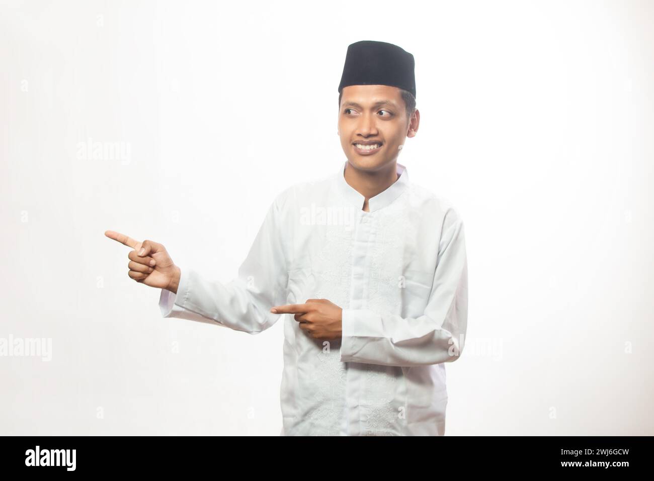 Brown skinned Asian Muslim man smiling sideways and both hands pointing ...