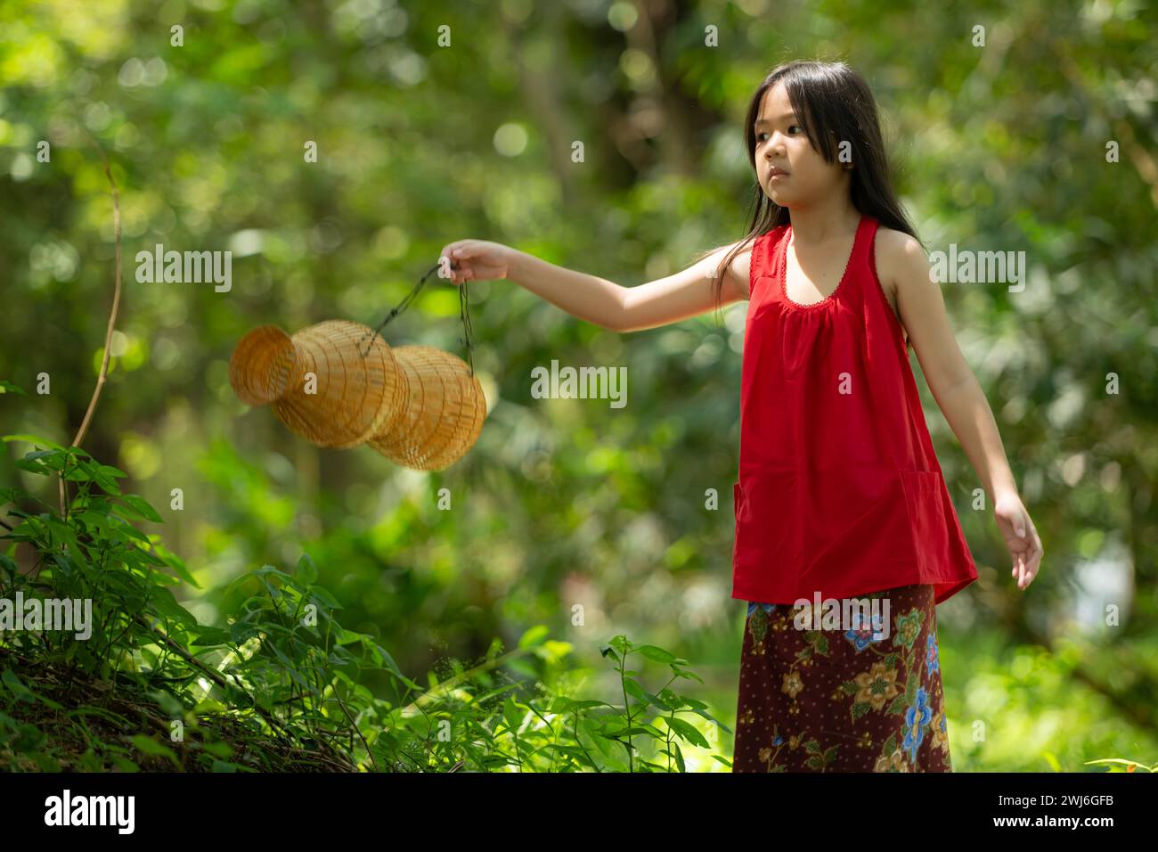 Little asian girl in red dress holding fishing equipment in the forest, Rural Thailand living ...