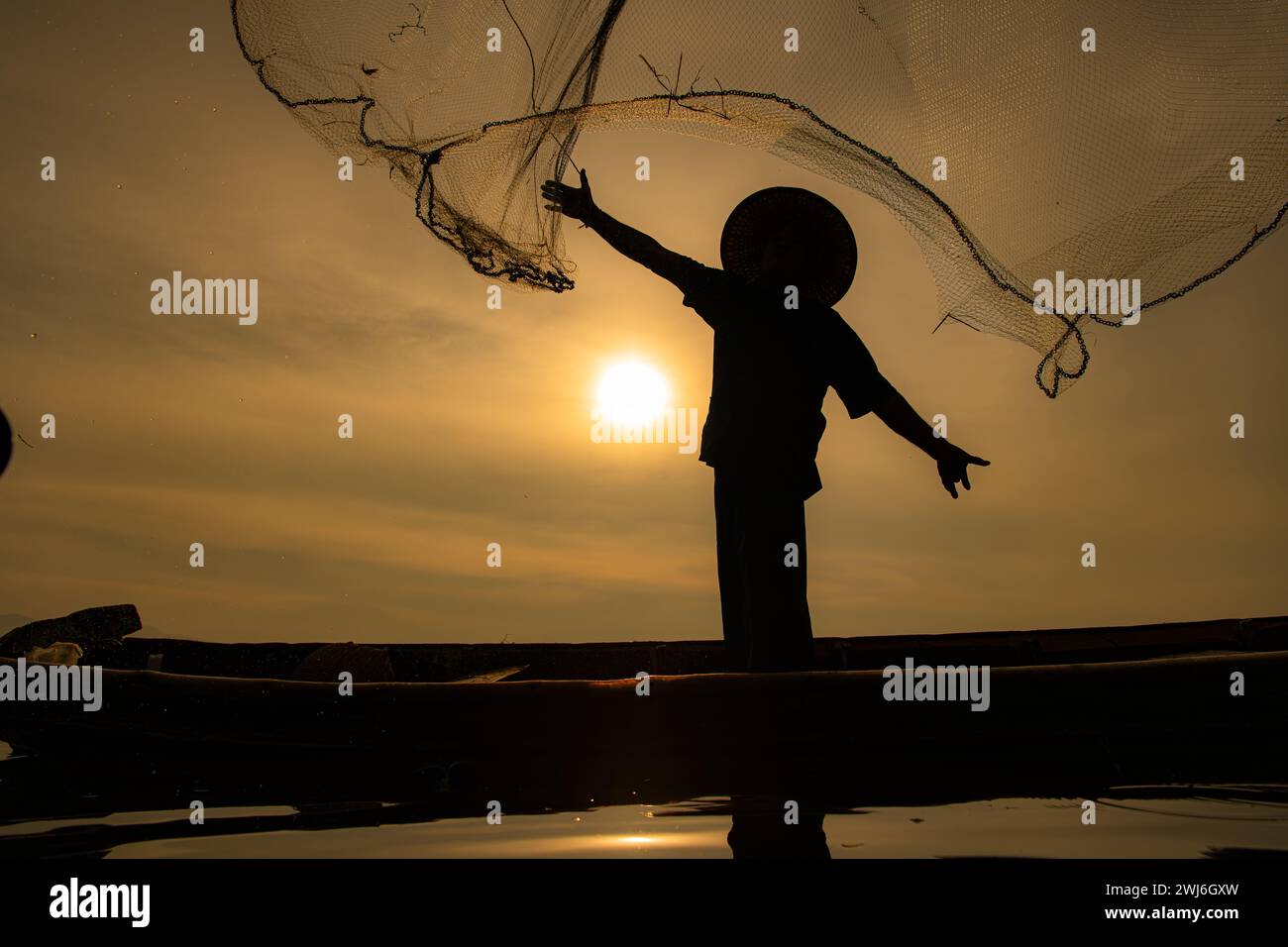 Silhouette of fisherman at sunrise, Standing aboard a rowing boat and ...