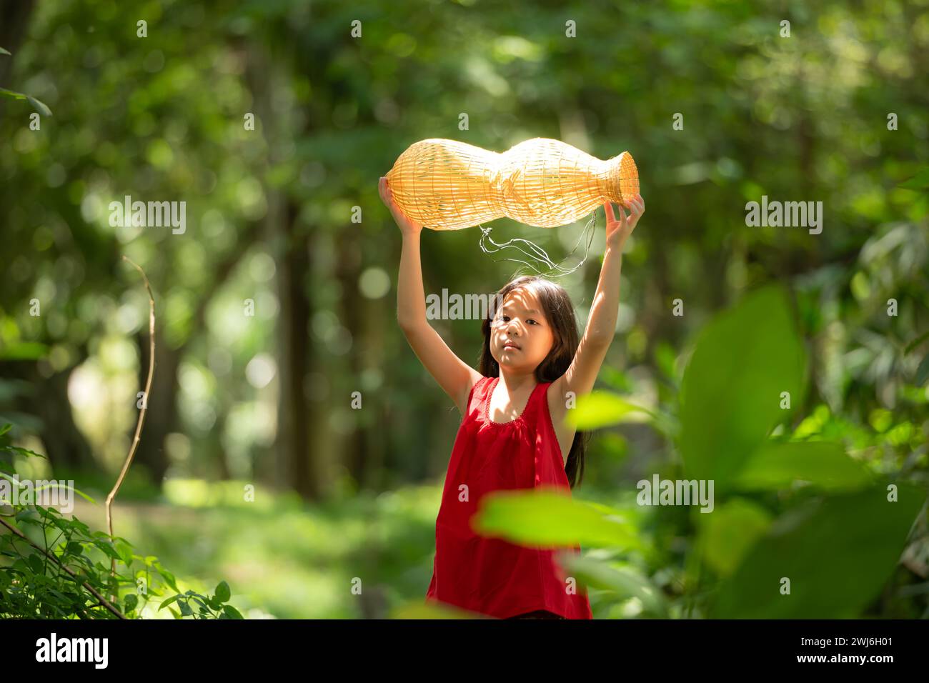 Little asian girl in red dress holding fishing equipment in the forest, Rural Thailand living ...