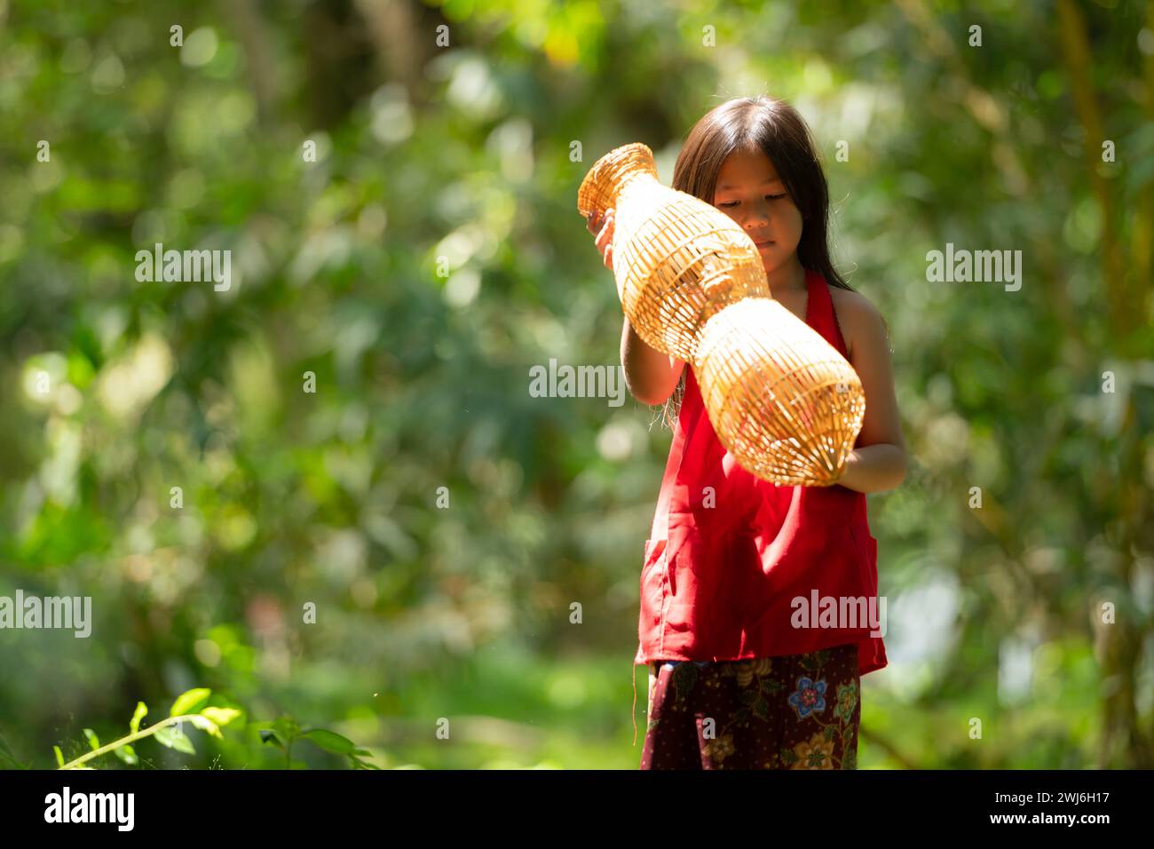 Little asian girl in red dress holding fishing equipment in the forest, Rural Thailand living ...